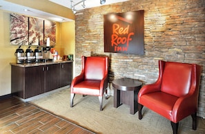 Área de recepção do Red Roof Inn, com parede de pedra, duas poltronas de couro vermelho, um canto para café e obras de arte nas paredes.