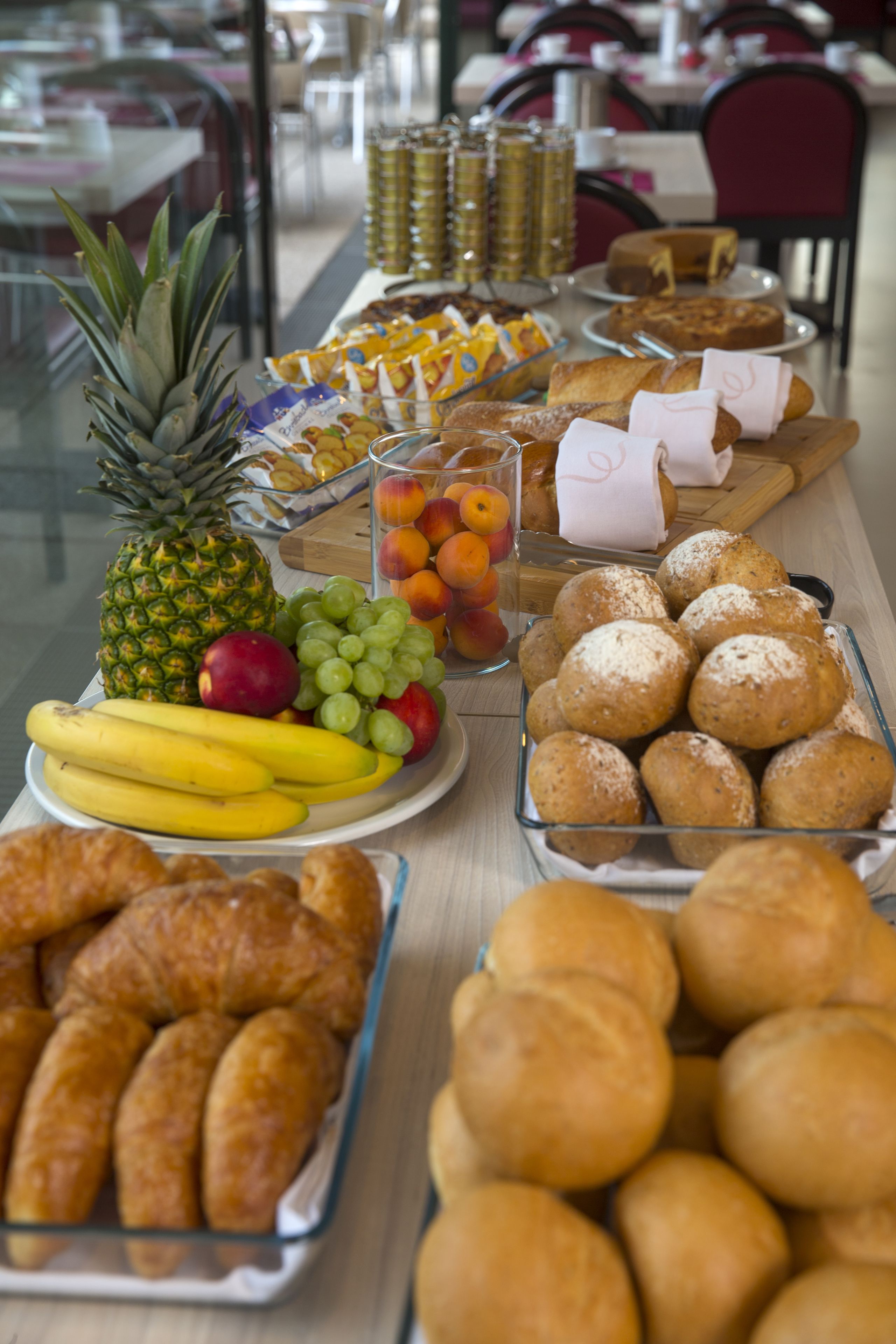 Uma mesa de buffet com diversos alimentos, incluindo frutas, doces e pães.