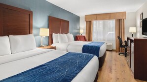 Quarto de hotel com duas camas, uma escrivaninha, uma cadeira, uma televisão e uma janela com cortinas.