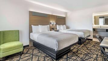 Quarto de hotel com duas camas, uma poltrona verde, uma escrivaninha e um espelho.