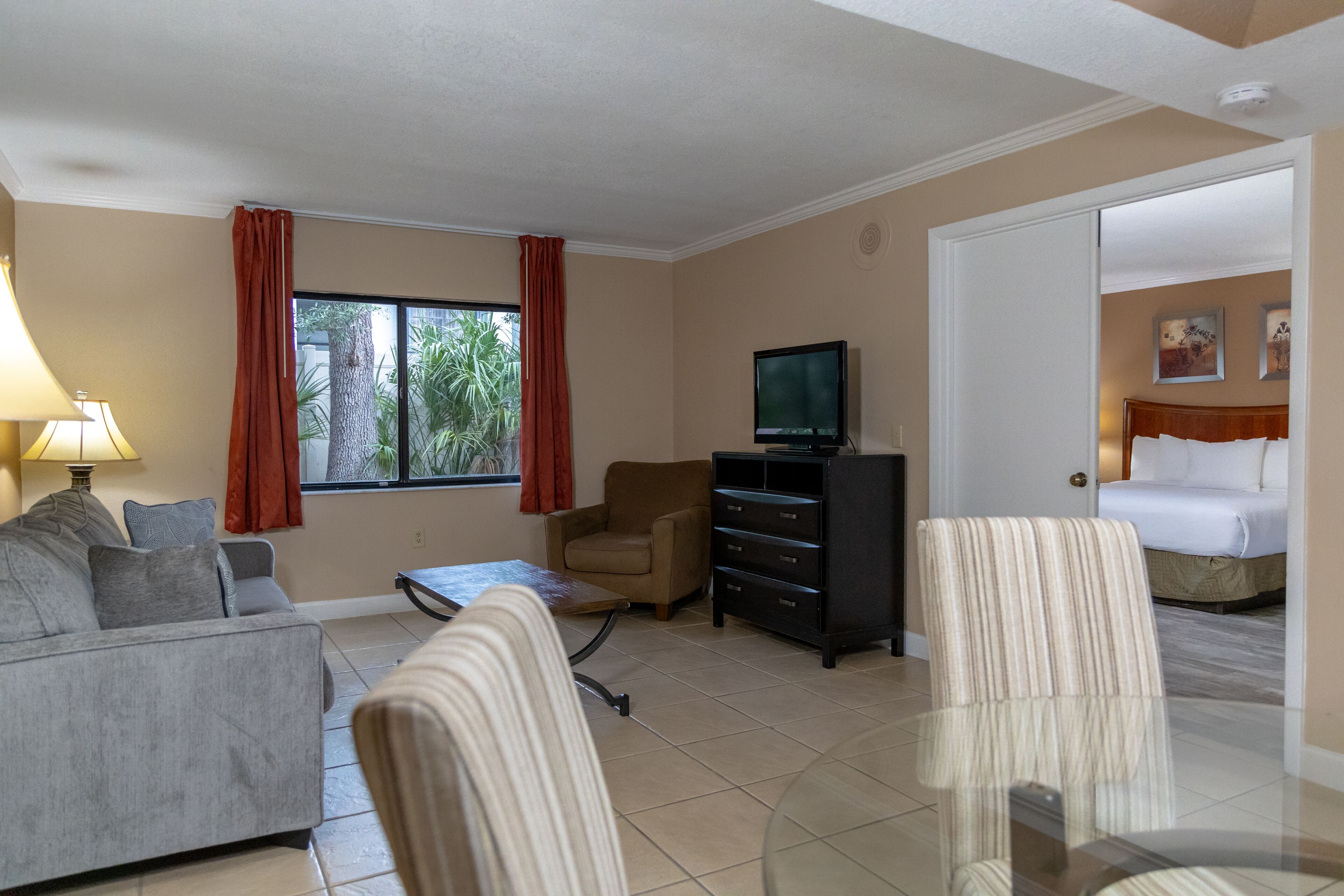 Quarto de hotel com sofá, poltrona, televisão e cama.
