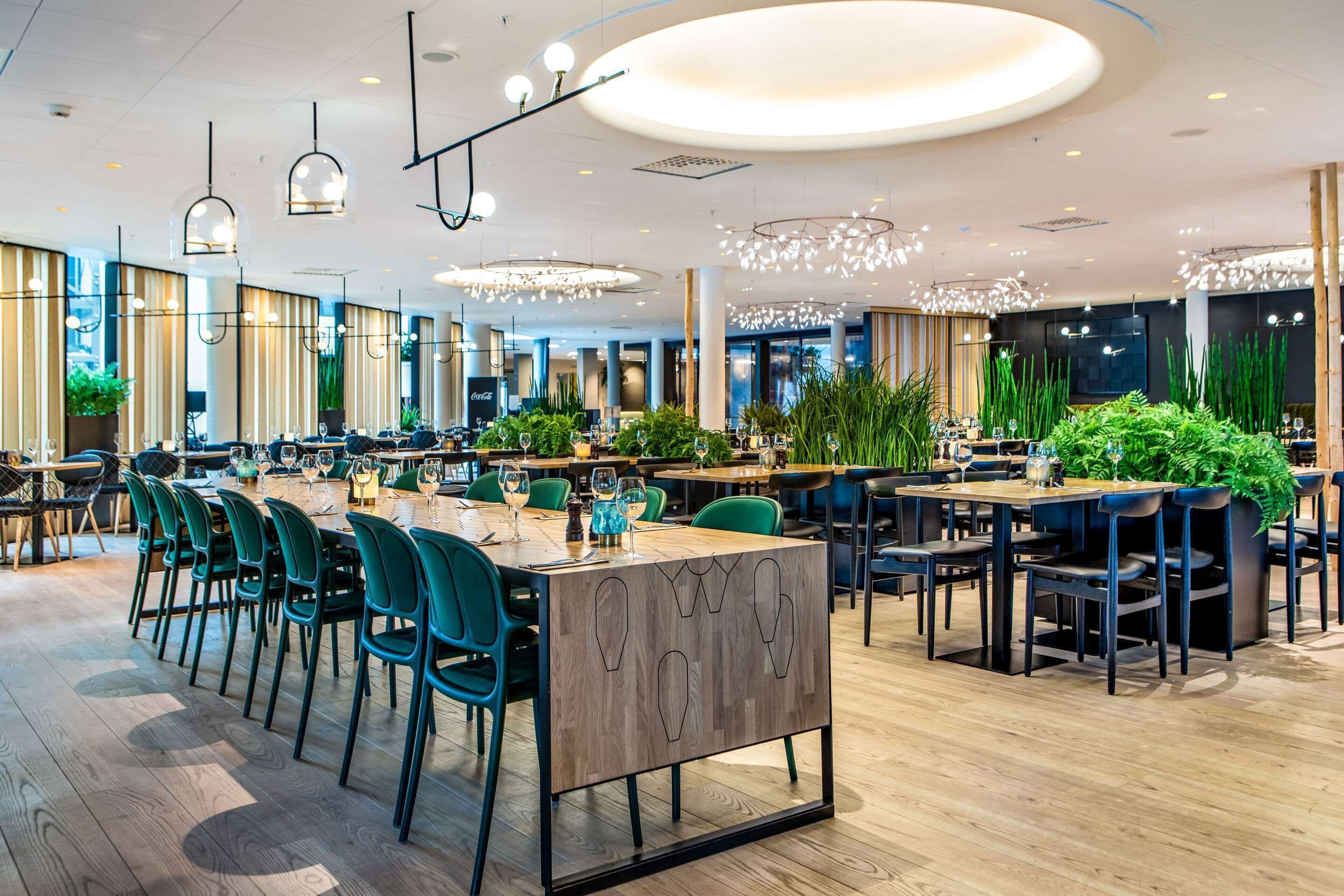 Um restaurante amplo, com pé-direito alto, iluminação moderna e diferentes opções de assentos.