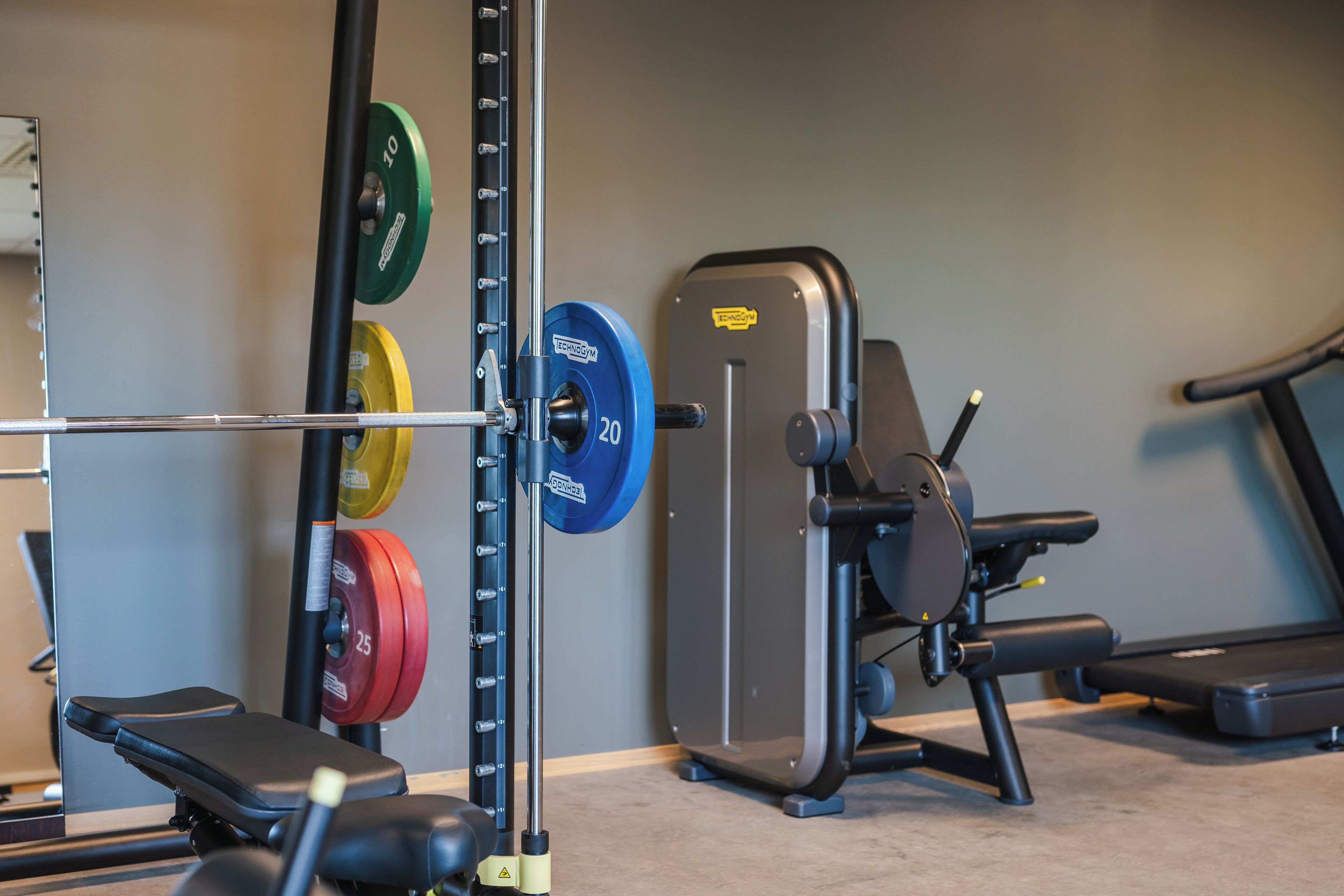 Uma área de musculação com banco, barra e anilhas.