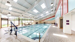 Piscina interior com pistas demarcadas, cadeira de salva-vidas e chão revestido de azulejos.