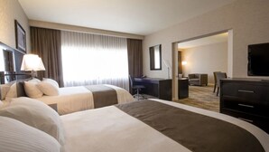 Quarto de hotel com duas camas, uma mesa, uma cadeira, uma televisão e uma janela grande com cortinas.