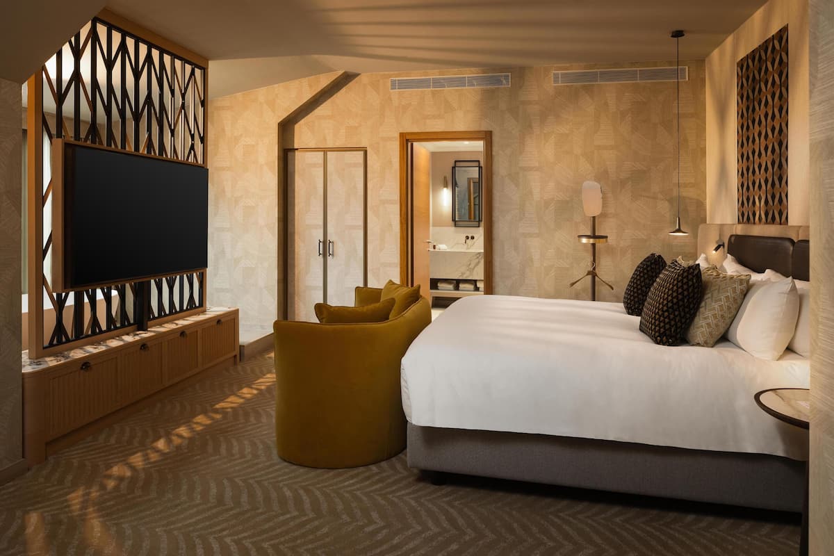 Quarto de hotel com cama, televisão, sofá e espelho.