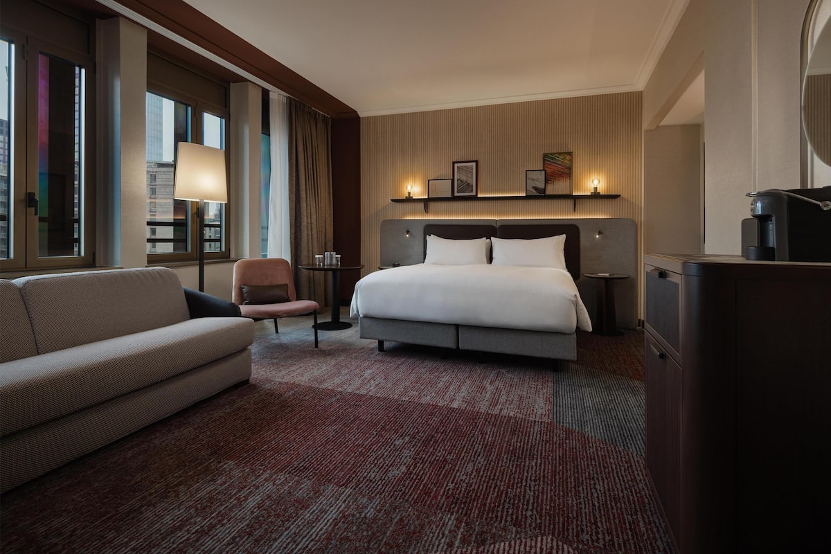Quarto de hotel com uma cama grande, um sofá, uma cadeira, uma escrivaninha e uma máquina de café.