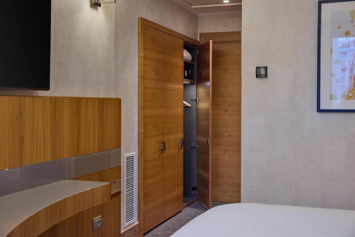 Quarto de hotel com guarda-roupa de madeira, penteadeira embutida e quadro na parede.