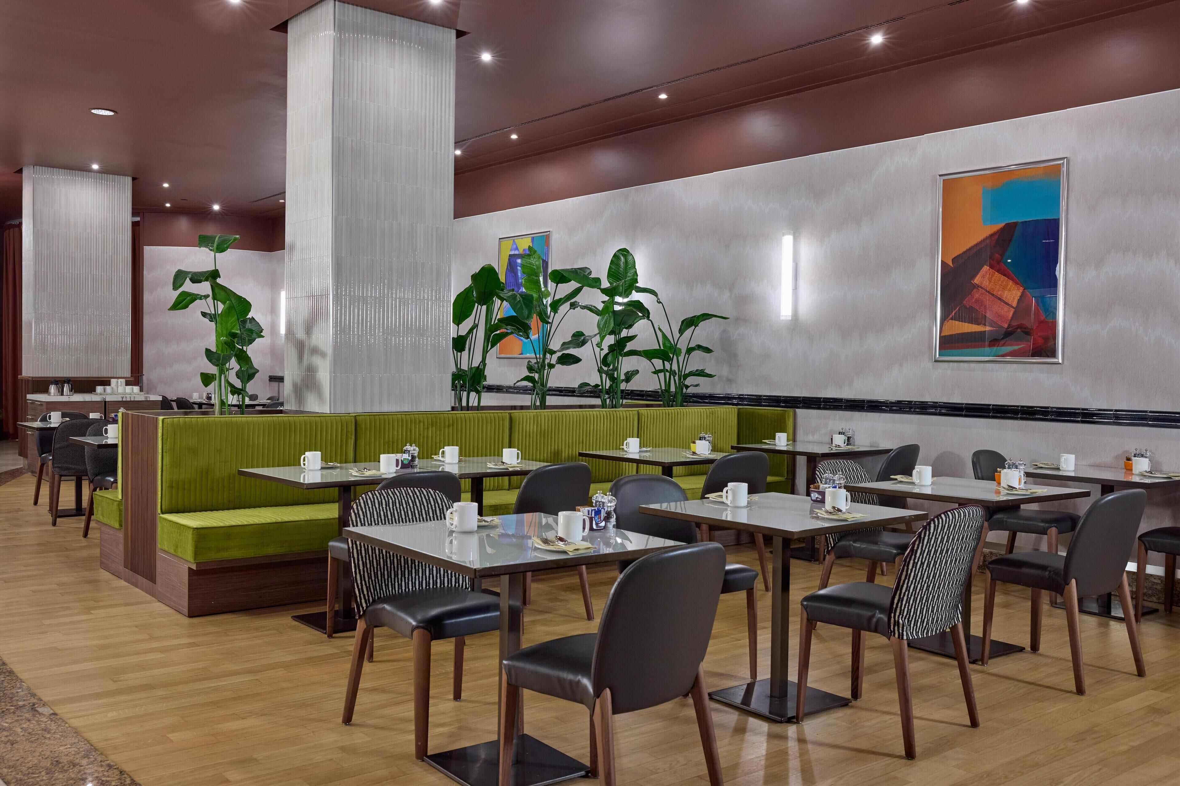 Uma sala de jantar moderna com assentos em verde, cadeiras pretas e uma parede de mármore com uma pintura abstrata colorida.