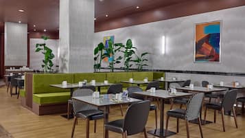 Uma sala de jantar moderna com assentos em verde, cadeiras pretas e uma parede de mármore com uma pintura abstrata colorida.