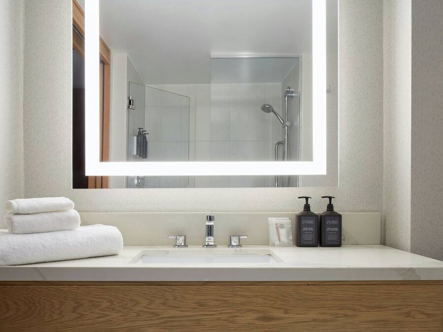 Um banheiro moderno com um espelho grande, pia branca e duas garrafas de shampoo.