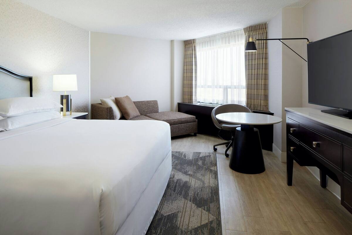 Quarto de hotel com uma cama grande, uma mesa, uma cadeira, uma televisão e uma pequena mesa.