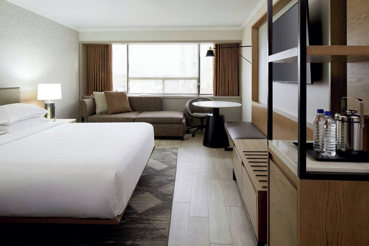 Quarto de hotel com uma cama grande, um sofá, uma mesa redonda pequena e uma televisão.