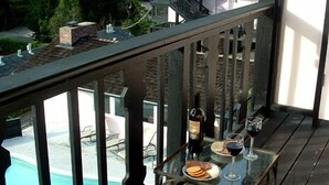 Uma varanda com mesa de vidro, uma garrafa de vinho e copos.