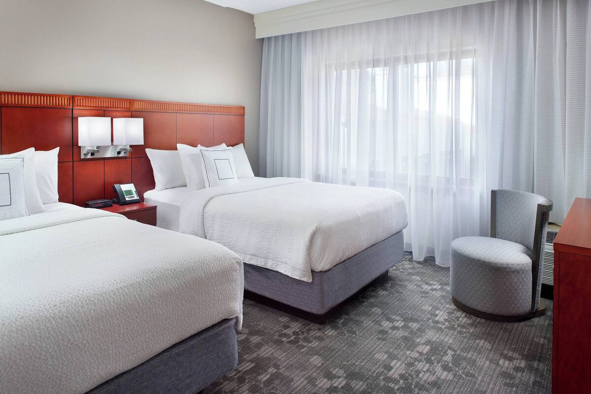 Quarto de hotel com duas camas, uma escrivaninha, uma cadeira e um telefone.