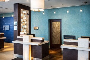 Uma área de recepção com design moderno, apresentando uma parede azul com textura, um balcão de madeira e um painel decorativo grande.