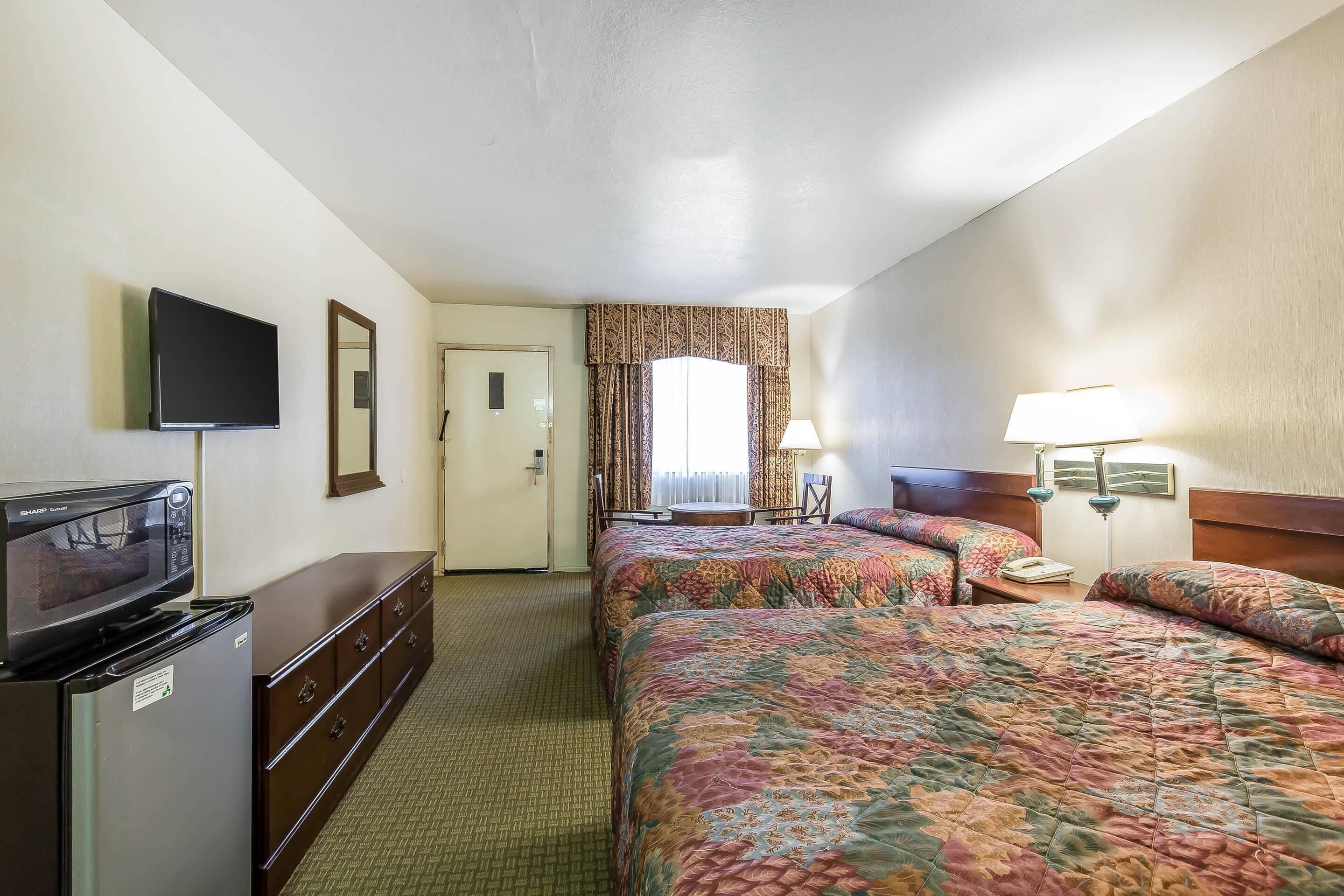 Quarto de hotel com duas camas, televisão, escrivaninha e abajur.
