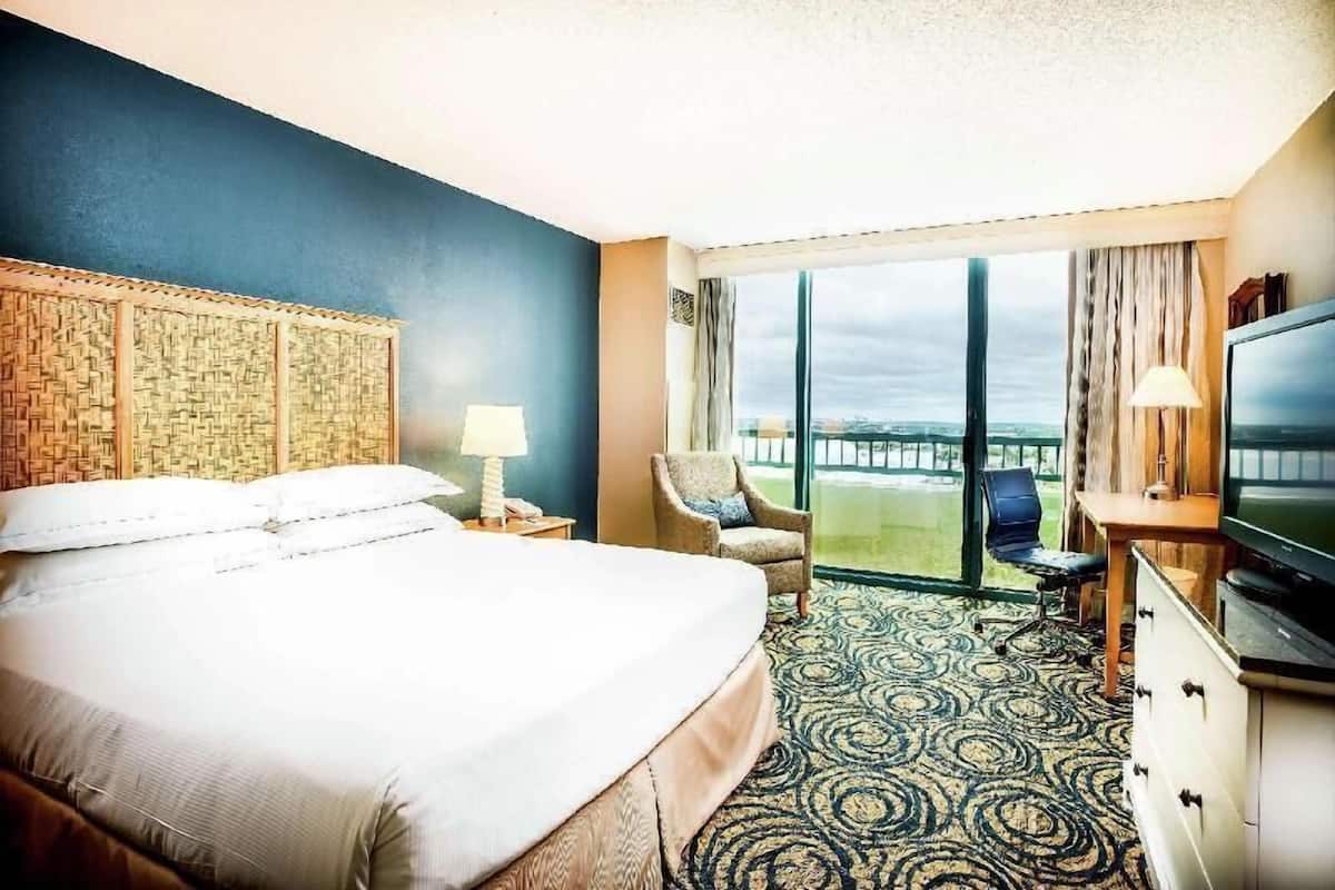 Quarto de hotel com uma cama grande, televisão, escrivaninha e vista da cidade pela janela.