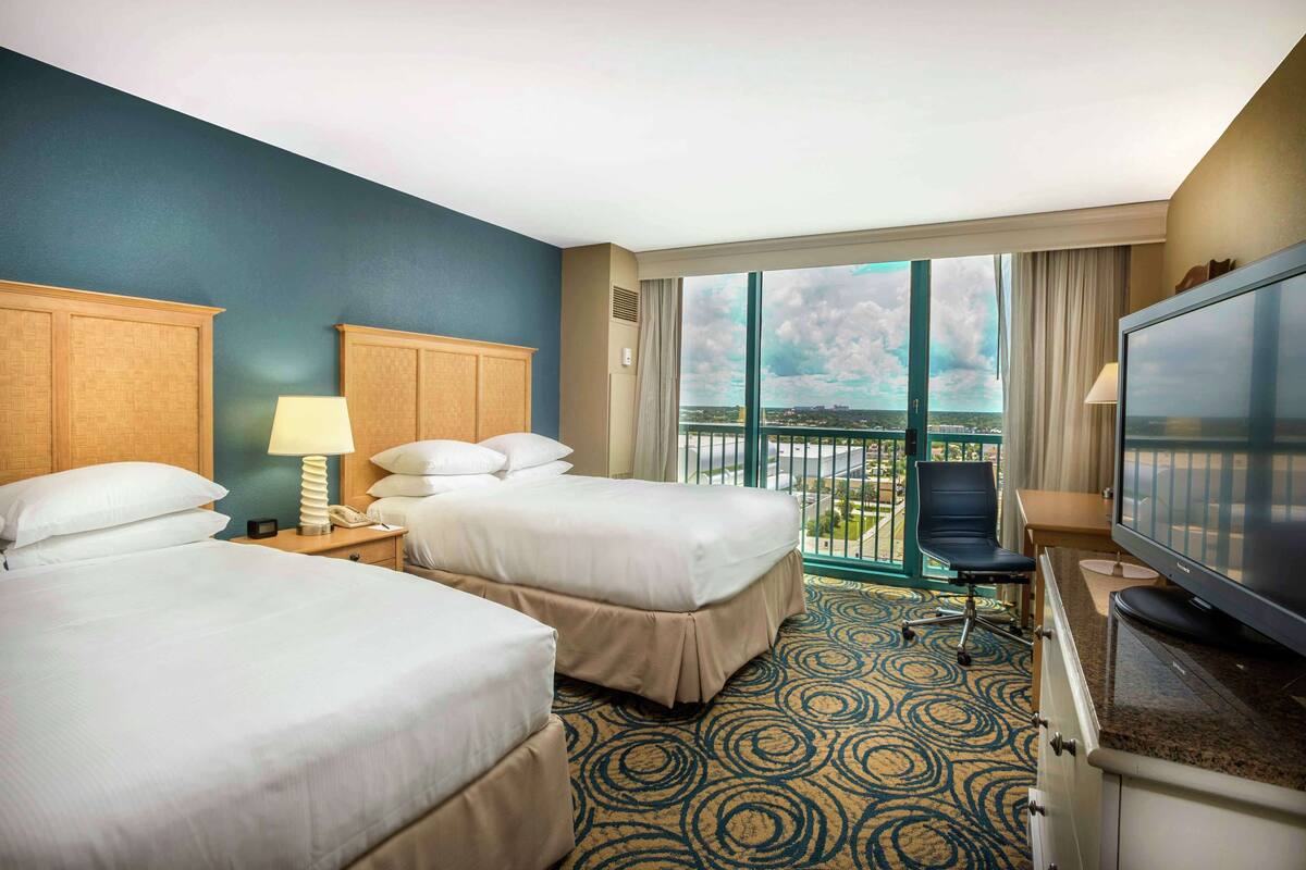 Quarto de hotel com duas camas, televisão, secretária e varanda com vista.