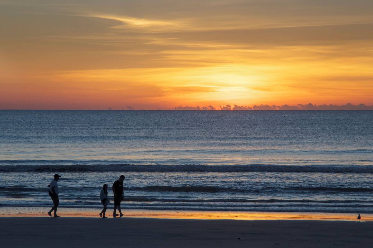 Uma praia com pessoas caminhando pela orla durante o pôr do sol.
