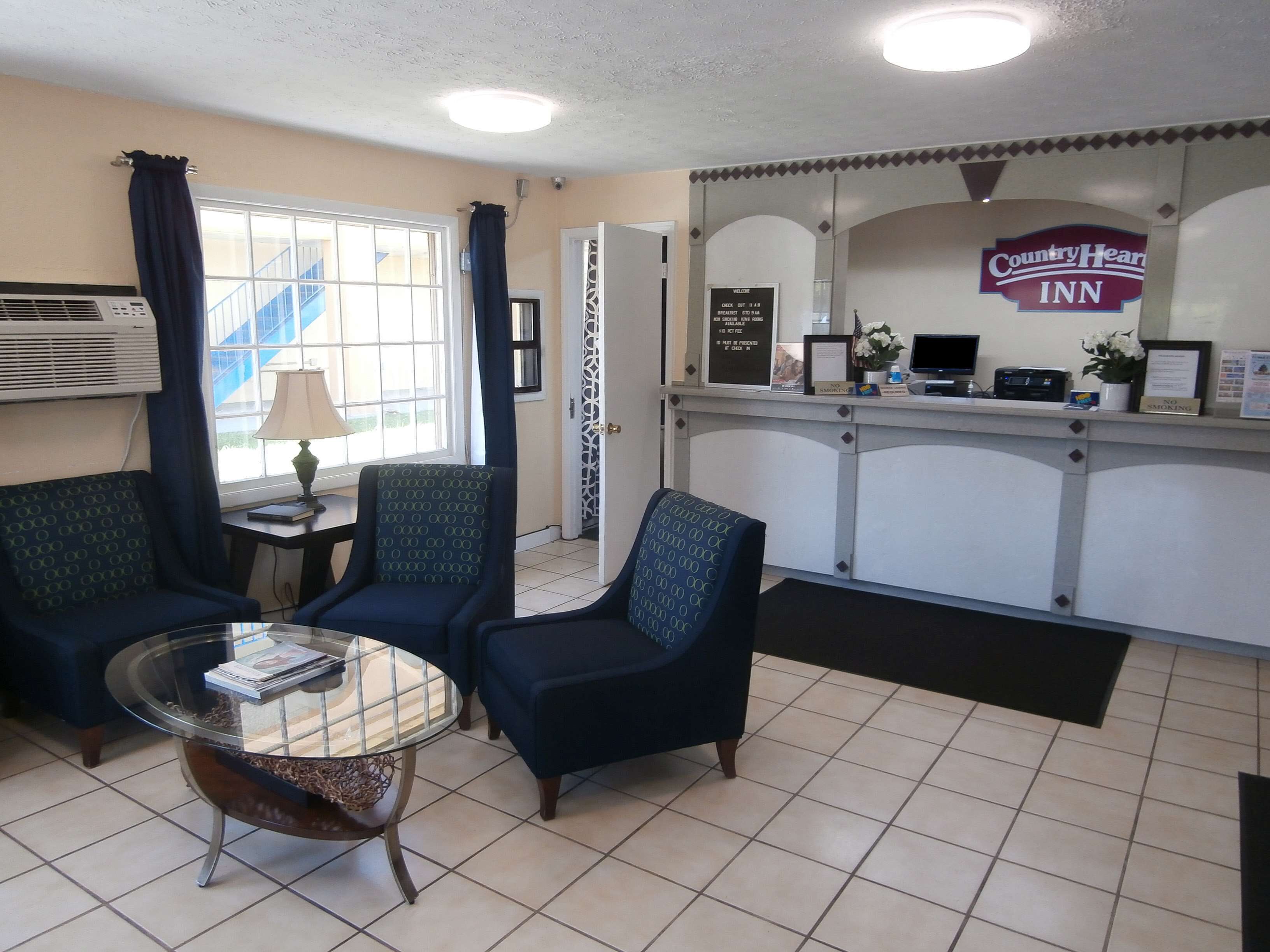 Recepção do Country Heart Inn, com balcão de check-in, duas poltronas, uma mesa de vidro e uma janela com cortinas.