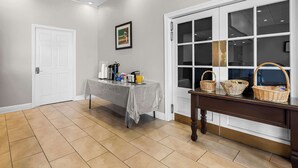 Um quarto limpo e bem iluminado, com piso de azulejos, uma mesa com itens de café da manhã e uma janela com cestos em um aparador.