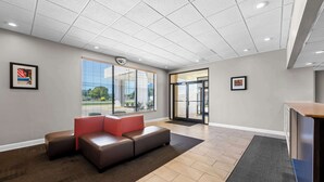 Um hall com um sofá de canto, um balcão de recepção e vista para o exterior por grandes janelas.