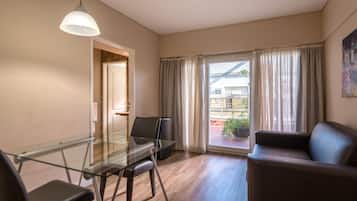 Uma sala de estar moderna com uma mesa de vidro, duas cadeiras, um sofá e uma janela grande com cortinas.