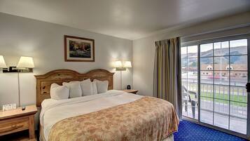 Quarto de hotel com uma cama grande, duas luminárias de cabeceira, um quadro na parede e vista para o exterior por uma janela ampla.