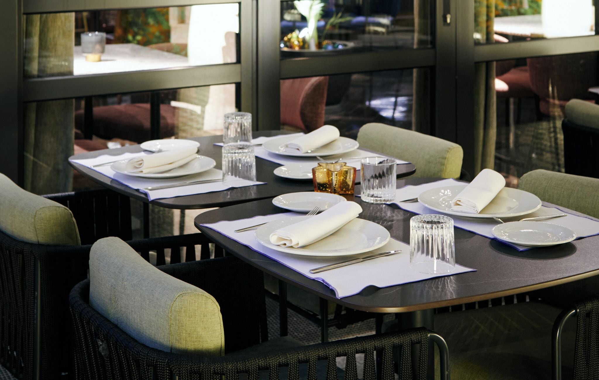 Uma sala de jantar com mesas dispostas para quatro pessoas, cada uma com pratos, talheres e copos.