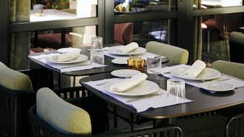 Uma sala de jantar com mesas dispostas para quatro pessoas, cada uma com pratos, talheres e copos.