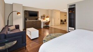 Quarto de hotel moderno com uma cama grande, um sofá, uma mesinha, uma escrivaninha e um guarda-roupa.
