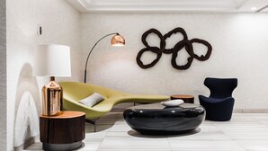 Uma sala de estar moderna com um sofá verde, uma mesa de centro preta, um abajur e uma obra de arte na parede.