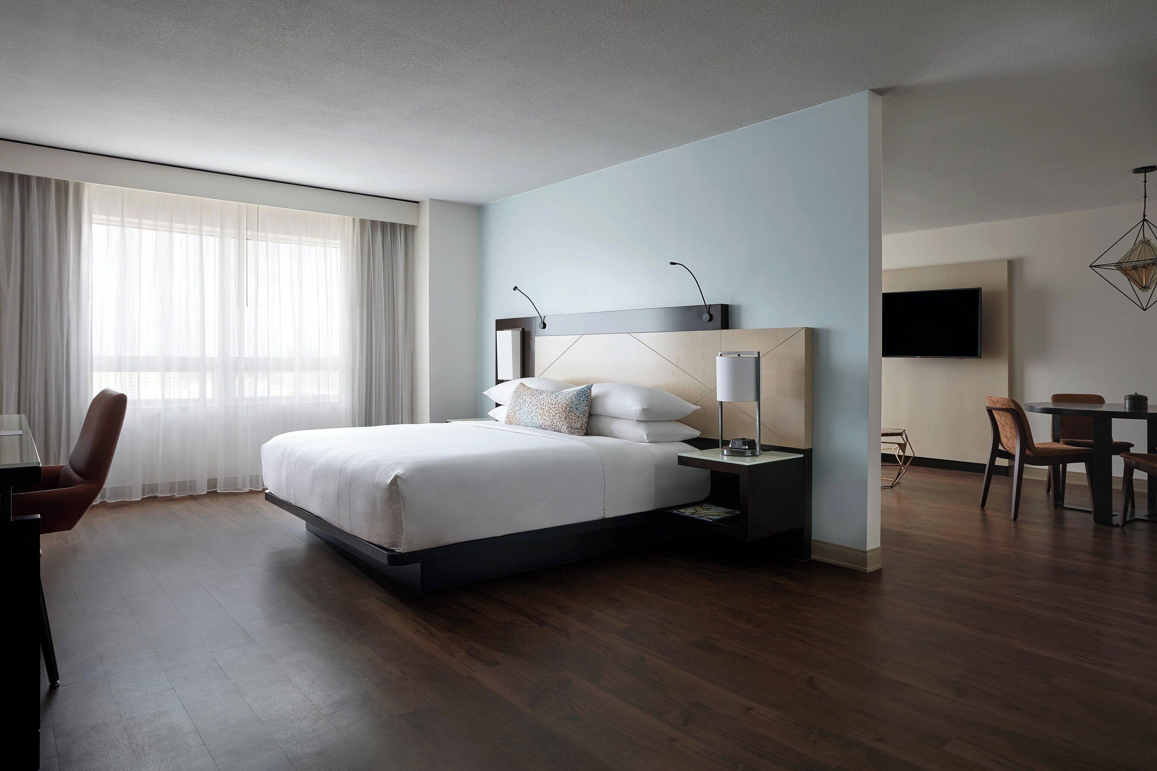 Quarto de hotel moderno com uma cama grande, uma escrivaninha, uma cadeira, uma televisão e um espaço de refeições.