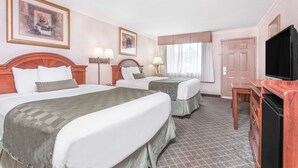 Quarto de hotel com duas camas, televisão, escrivaninha e guarda-roupa.