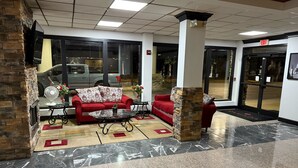 Um saguão com um sofá vermelho, uma mesa de centro de vidro e um ventilador. Há pilares de pedra e um piso de azulejos.