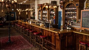Um bar com um balcão extenso, vários bancos e uma variedade de garrafas e copos.