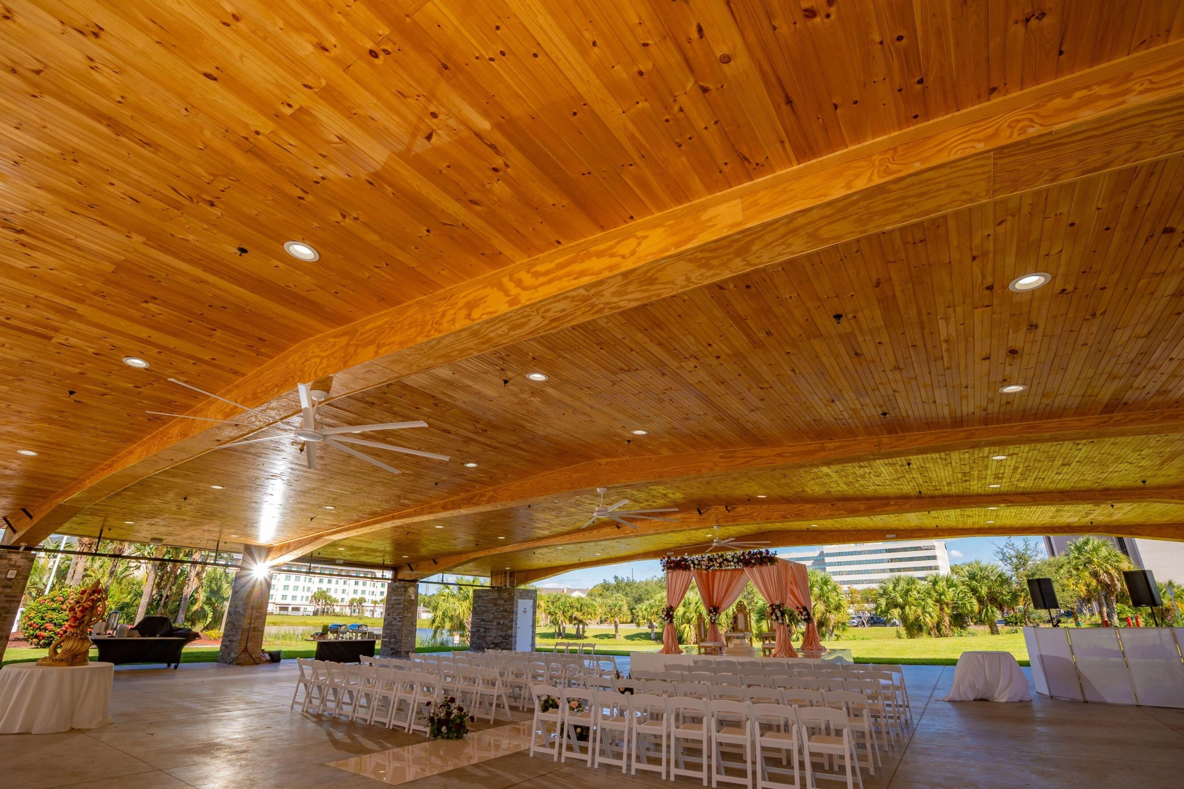Um espaço interior com teto de madeira, fileiras de cadeiras brancas e um palco com cortinas.