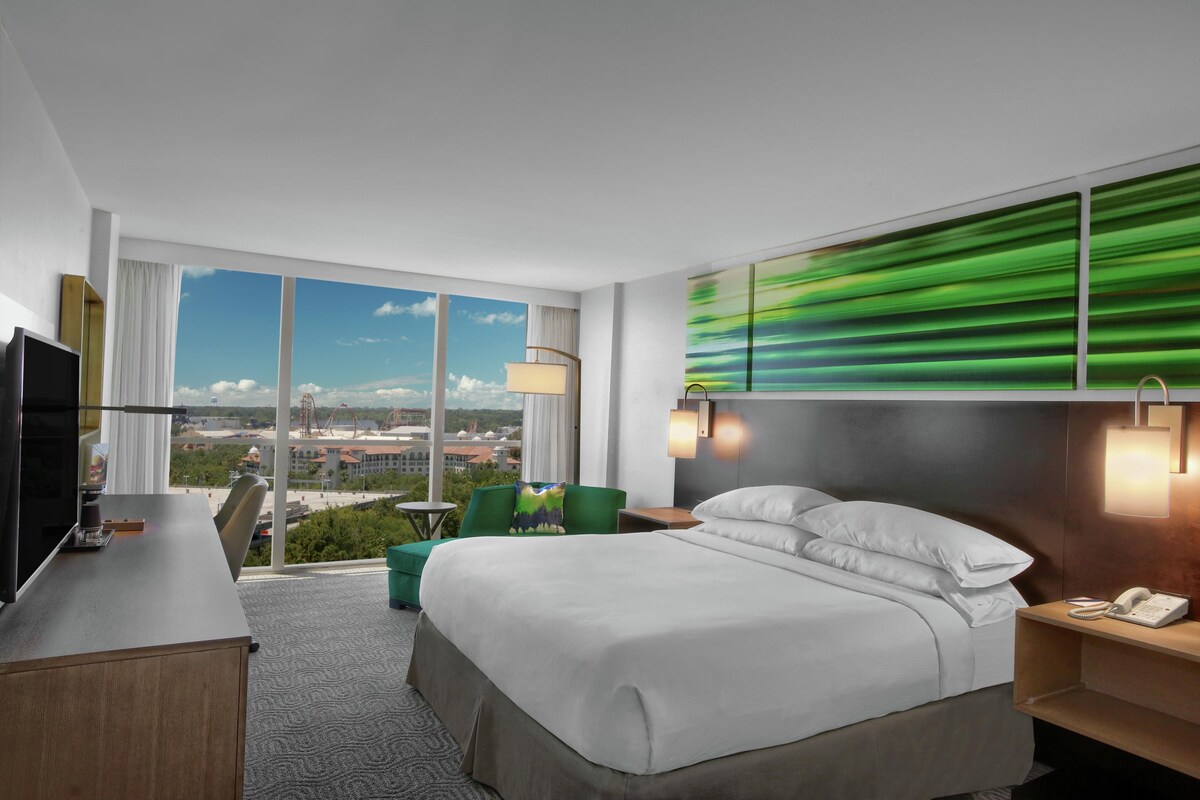 Quarto de hotel com cama grande, escrivaninha, cadeira, televisão, telefone e vista para a cidade.