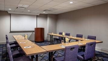 Uma sala de conferências com uma mesa comprida, cadeiras, uma tela de projetor e um pilar de madeira.