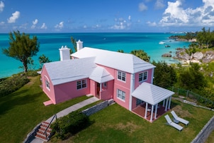 Uma casa rosa com telhado branco, varanda coberta e vista para o oceano.
