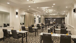 Um salão de refeições de hotel com várias mesas, cadeiras, lustres no teto e piso estampado.
