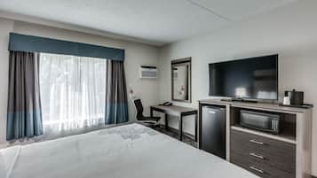 Quarto de hotel com cama, escrivaninha, cadeira, televisão, micro-ondas e um pequeno frigorífico.
