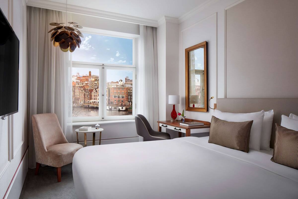 Quarto de hotel com cama, escrivaninha, cadeira, TV e janela com vista para a cidade.