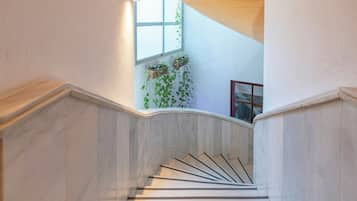 Escadaria com paredes de mármore, corrimão de madeira e janela com plantas penduradas.