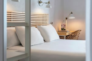 Uma cama bem arrumada com lençóis brancos, cabeceira de madeira e duas luminárias laterais.