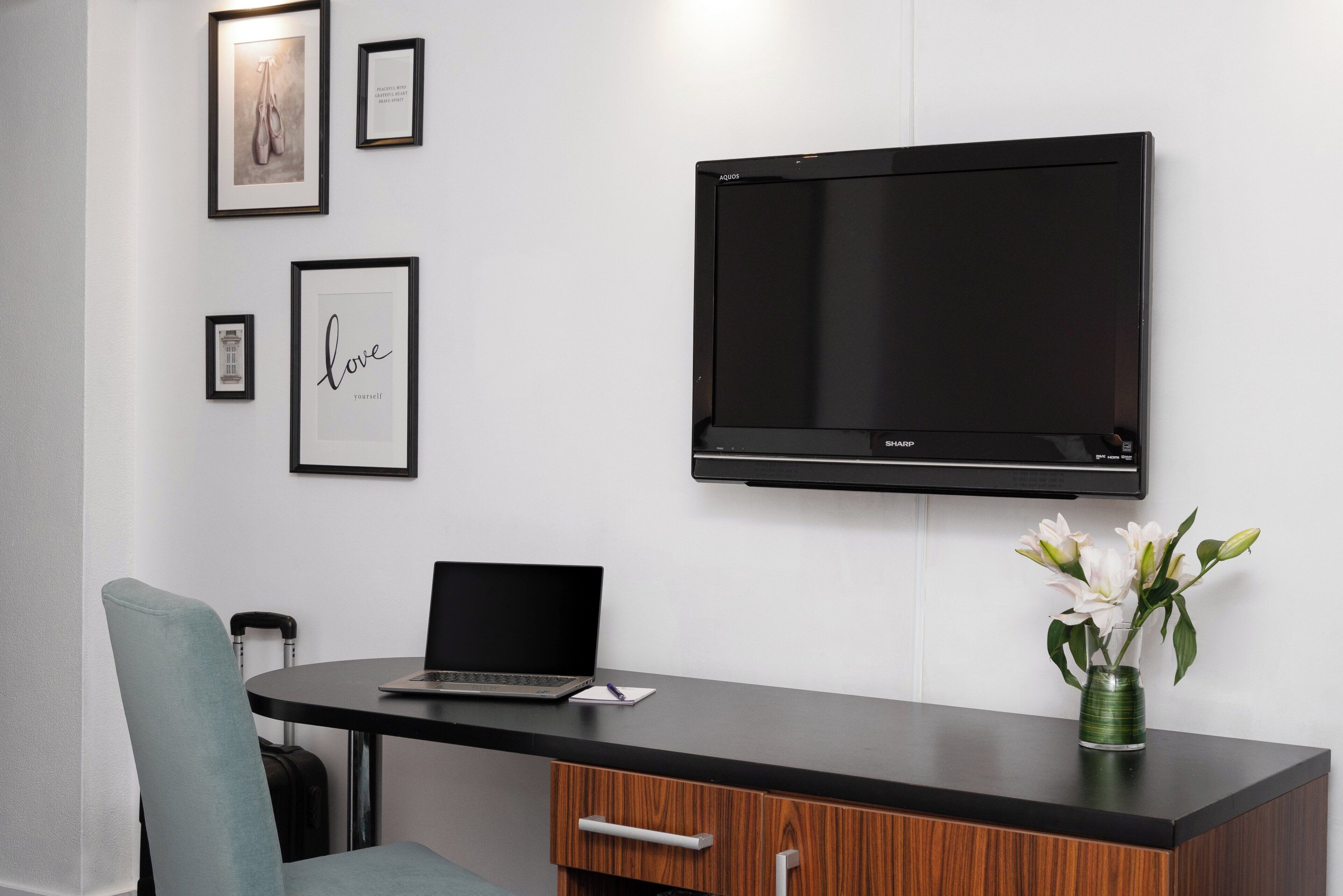 Quarto moderno com escrivaninha preta, laptop, TV e quadros na parede.