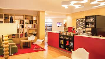 Um saguão de hotel moderno com um balcão de recepção vermelho, cadeiras brancas, uma estante de madeira e um tapete vermelho.