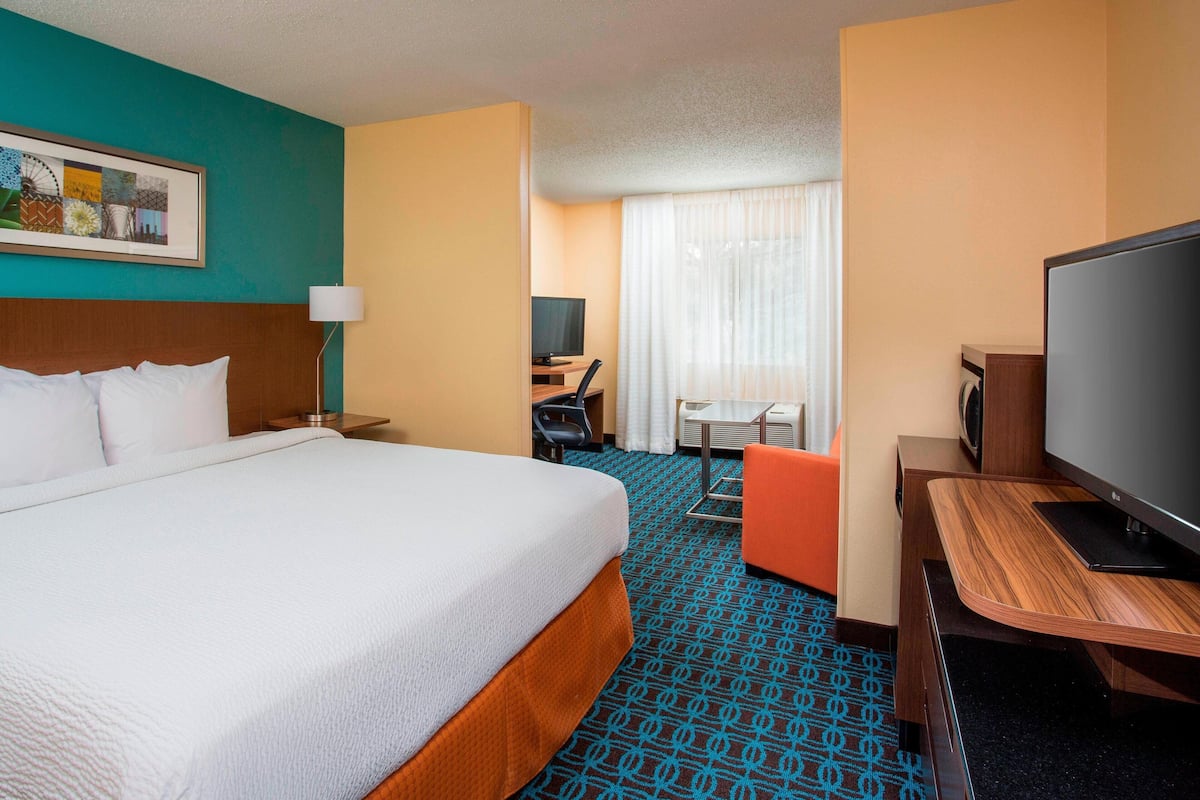 Quarto de hotel com uma cama grande, uma escrivaninha com computador, televisão e janela com cortinas.