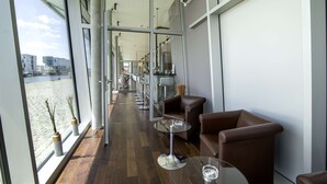 Interior moderno com vista para um rio, assentos de couro e um longo corredor com mesas e cadeiras.